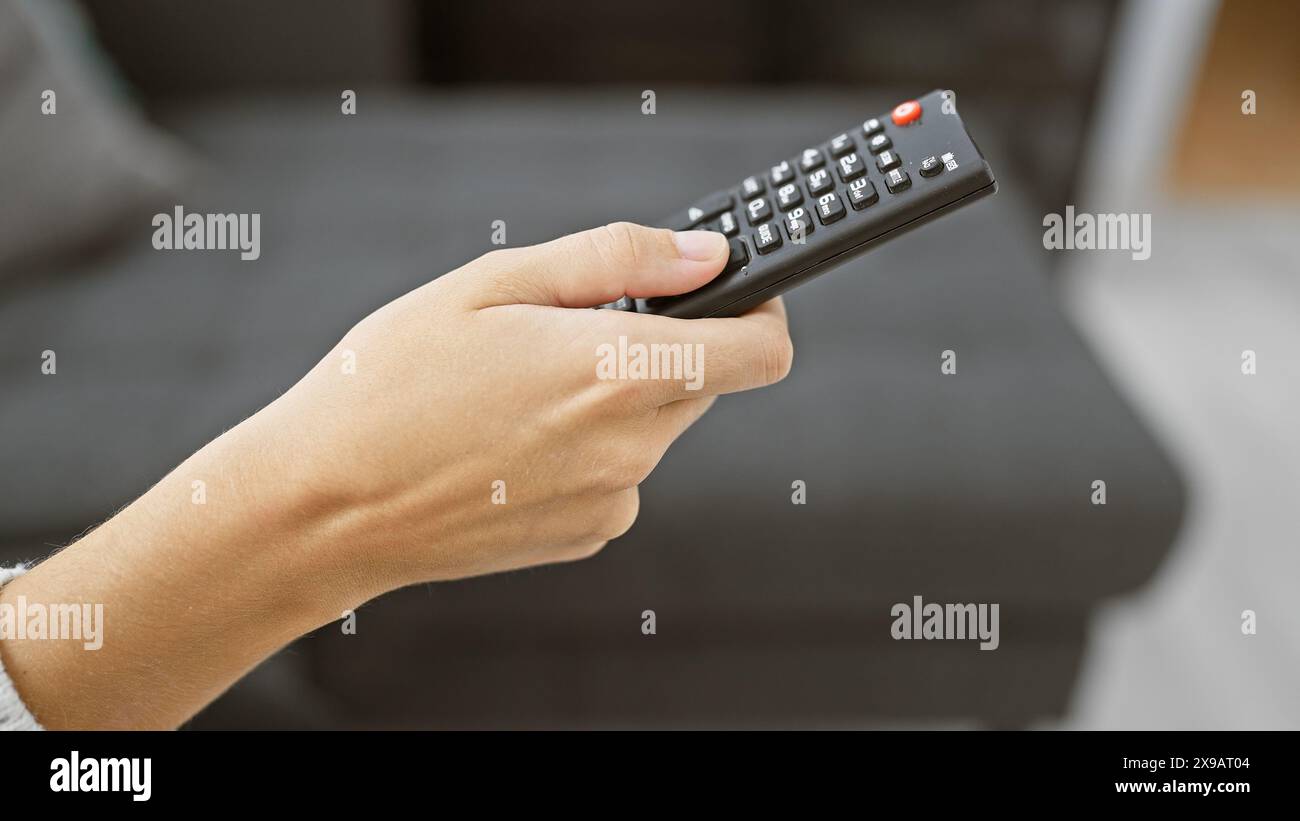 A person holding a remote control while sitting on a couch inside a ...