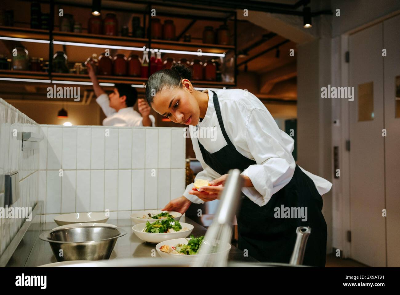 Female chef holding lemon slice while garnishing salad at commercial ...
