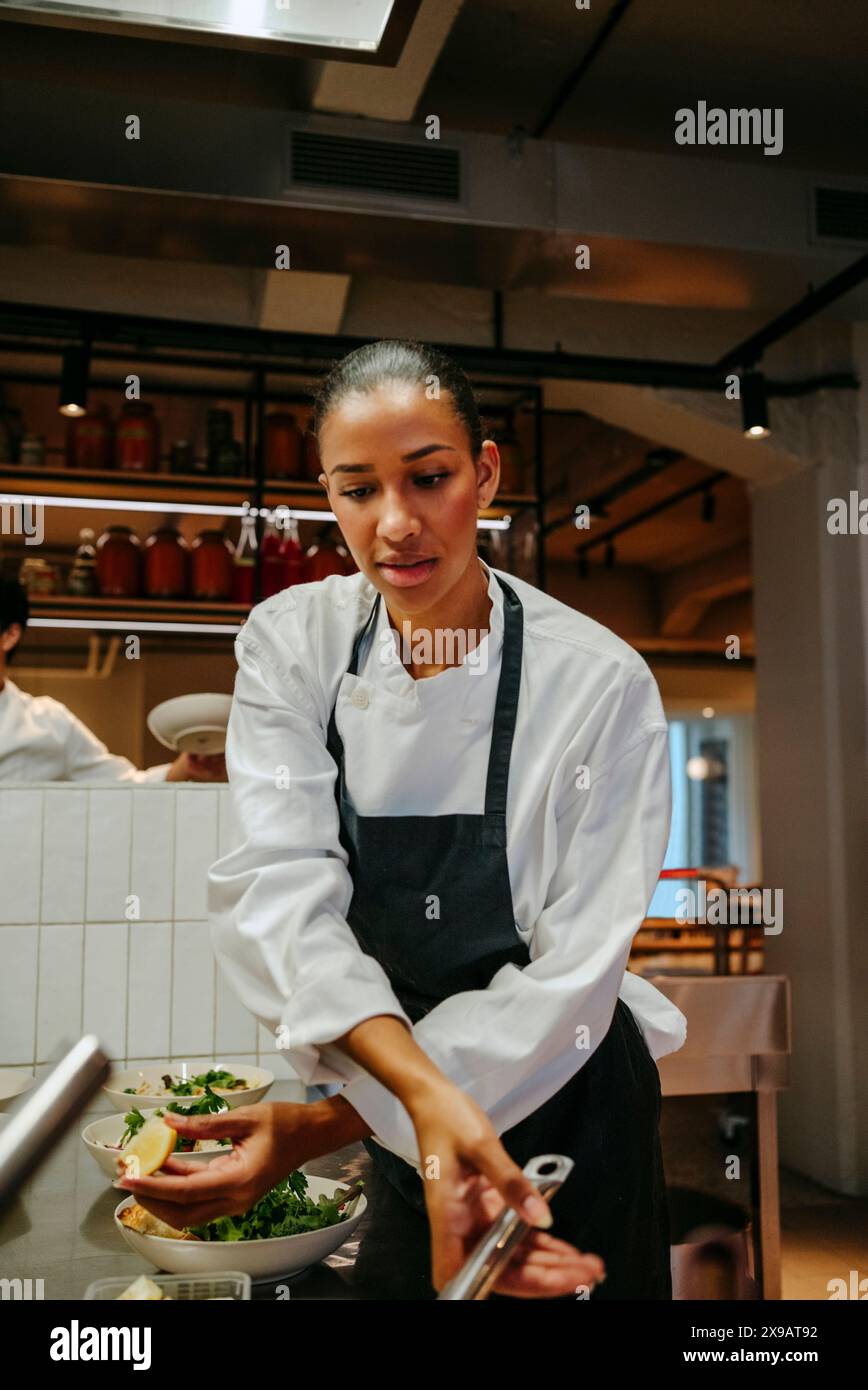 Focused female chef multi-tasking in commercial kitchen at restaurant ...