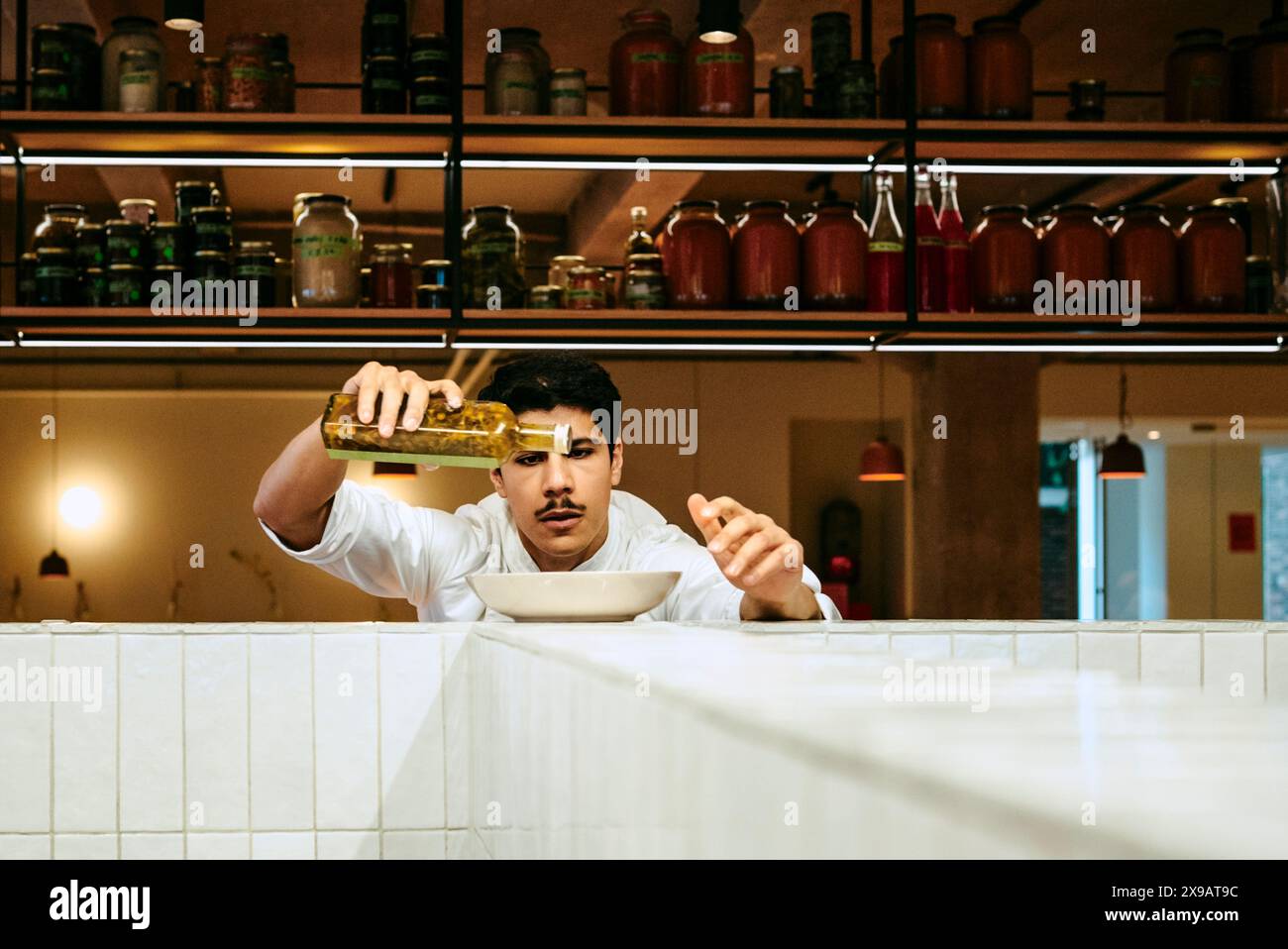 Focused male chef pouring ingredient in bowl at commercial kitchen in ...