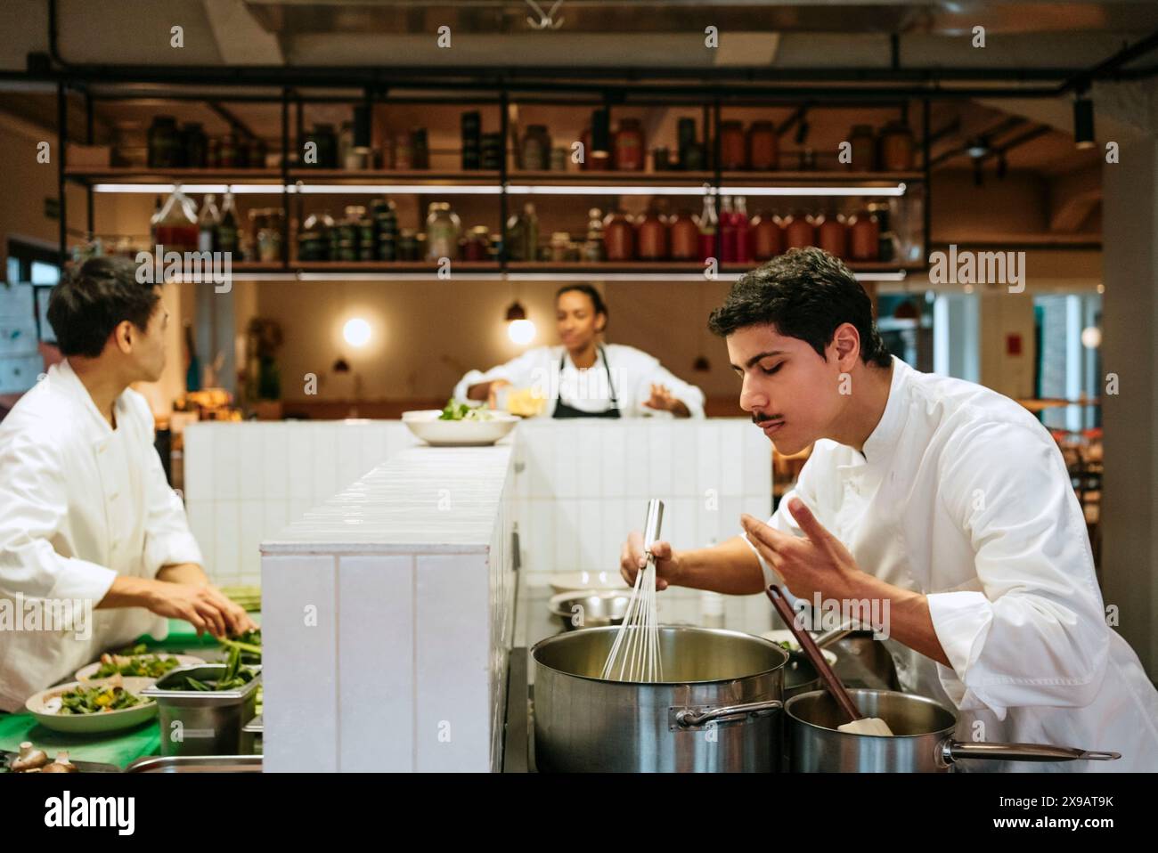 Male chef smelling food aroma while cooking with colleagues in ...