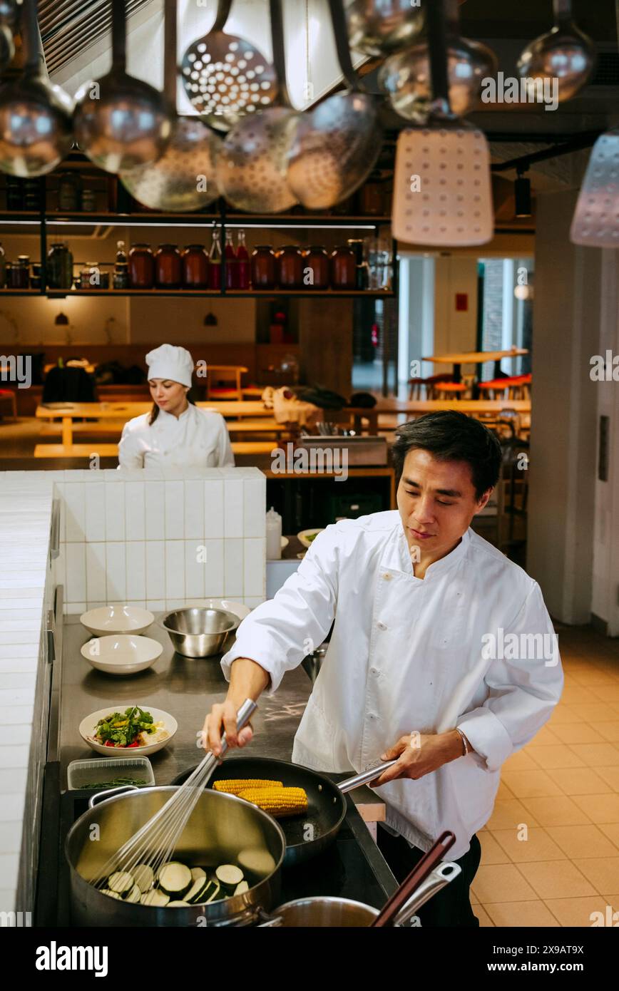 Male chef cooking zucchini with wire whisk in commercial kitchen Stock ...