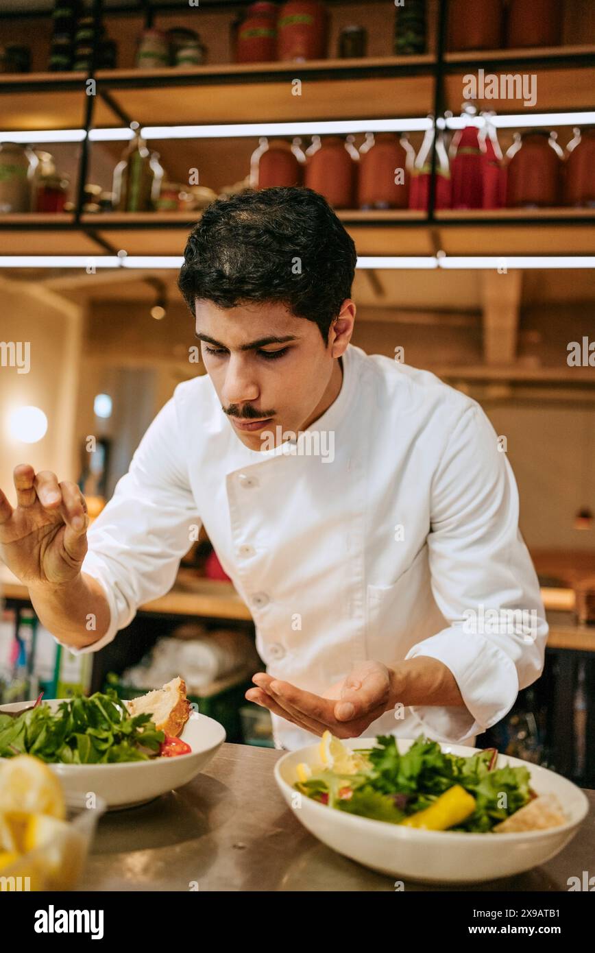 Male chef sprinkling salt on salad at commercial kitchen Stock Photo ...