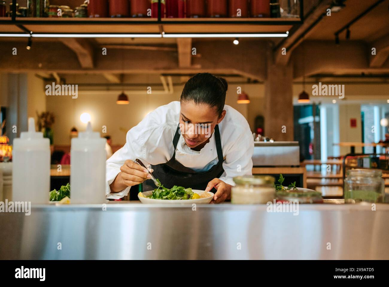 Focused female chef arranging cilantro using tweezers in commercial ...
