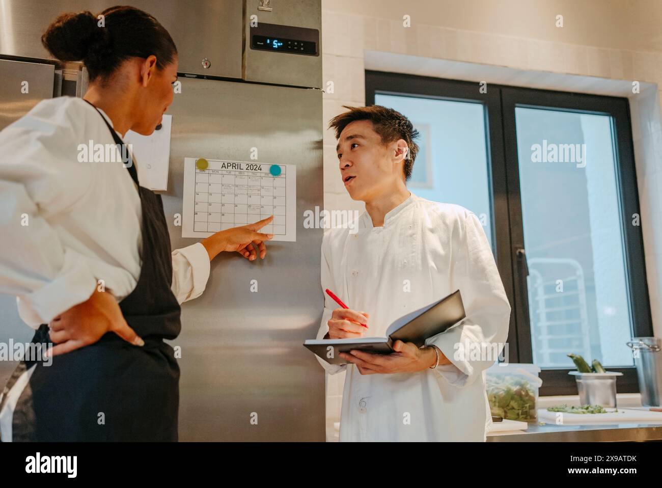 Female chef pointing at calendar while discussing with male chef ...