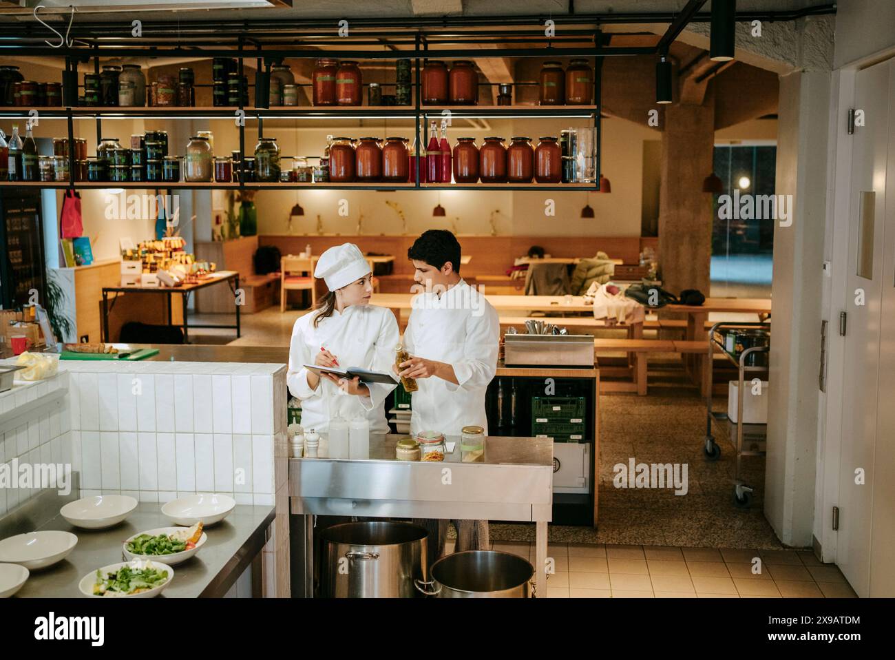 Female chef holding diary discussing inventory with male coworker while ...