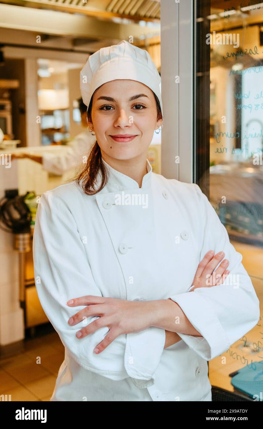 Happy female chef with arms crossed standing at door in commercial ...