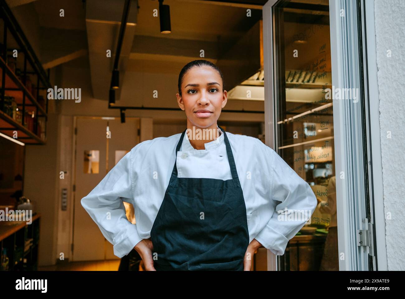 Portrait of female chef standing on door with hand on hip at commercial ...