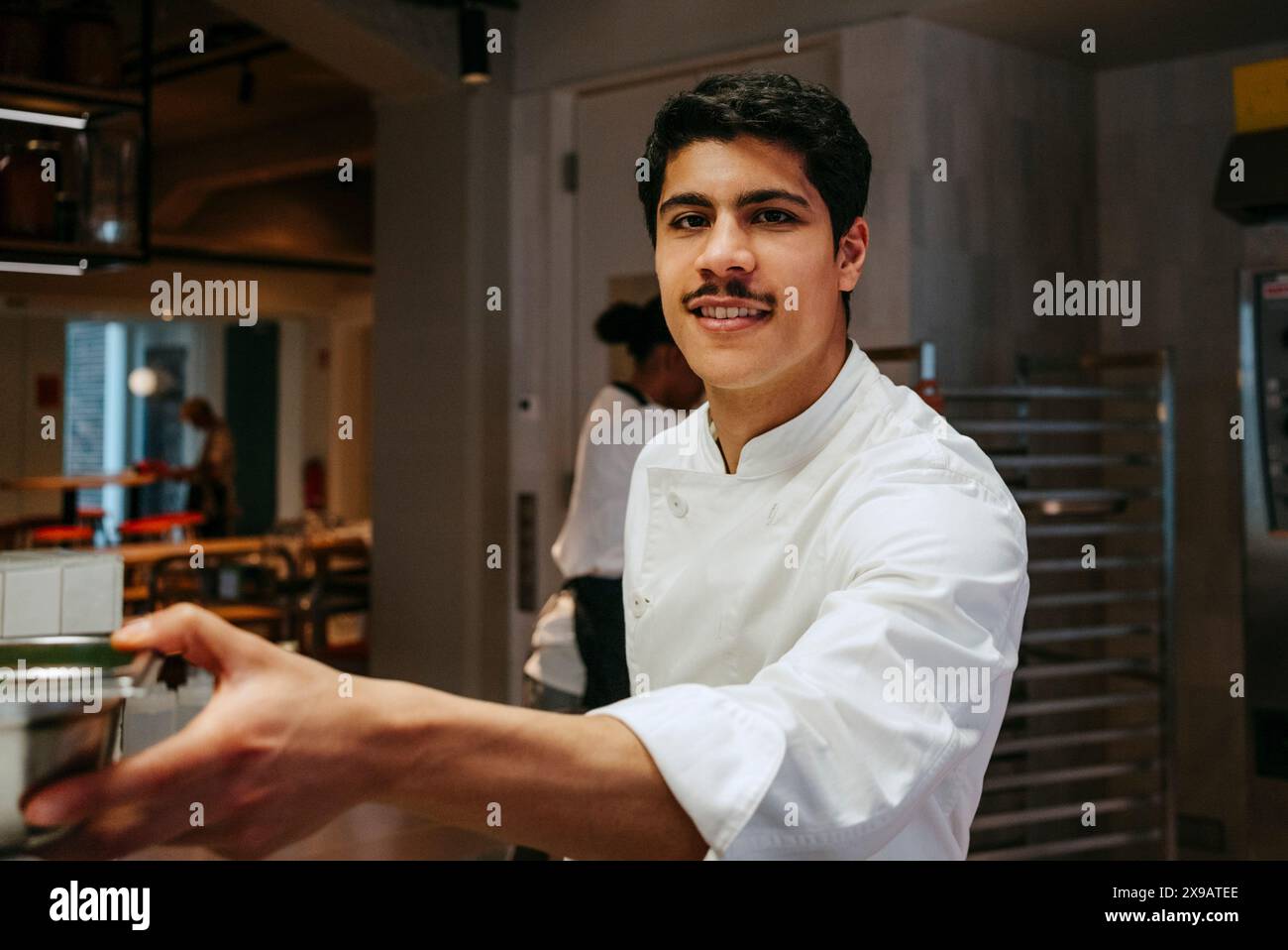 Portrait of happy male chef with mustache working in commercial kitchen ...