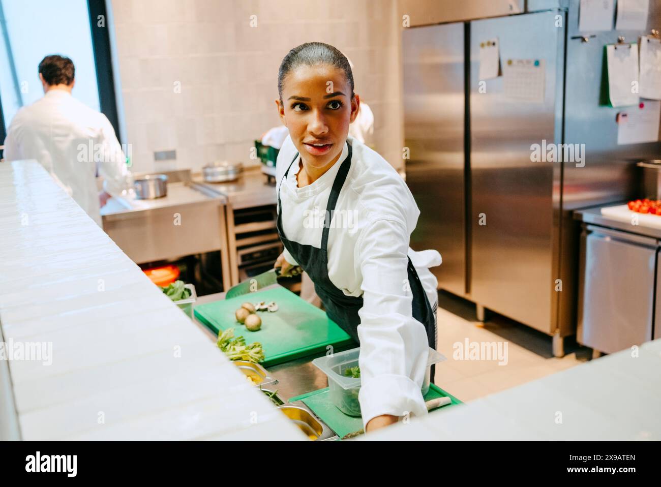 Female chef looking away while working in commercial kitchen with ...