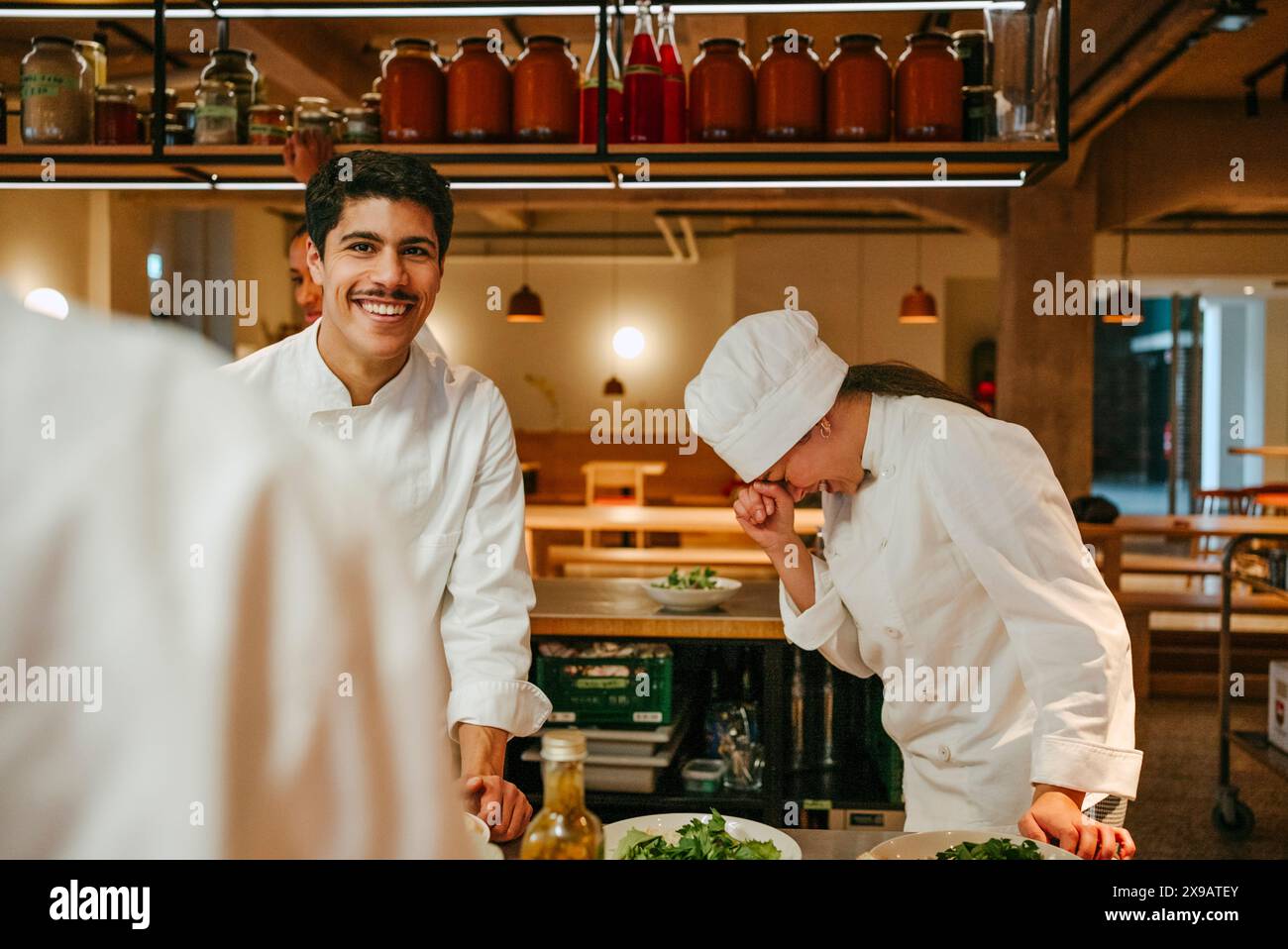 Male and female chef laughing with coworkers while working in ...