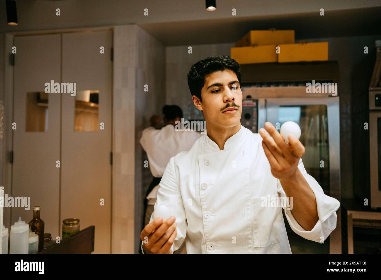 Male chef checking quality of egg in hand while standing in commercial ...