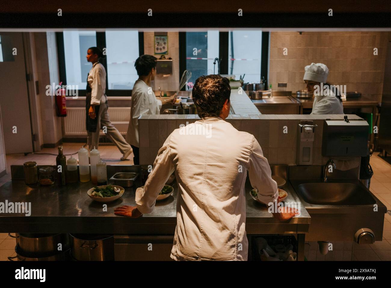 Rear view of male chef standing near kitchen counter with coworkers ...
