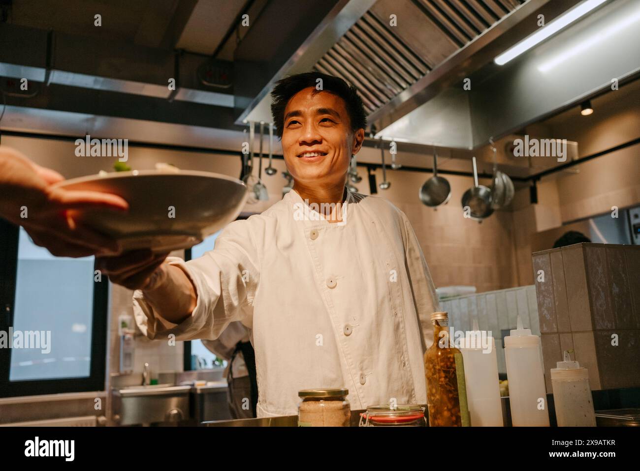 Happy male chef passing salad bowl to colleague while working in ...