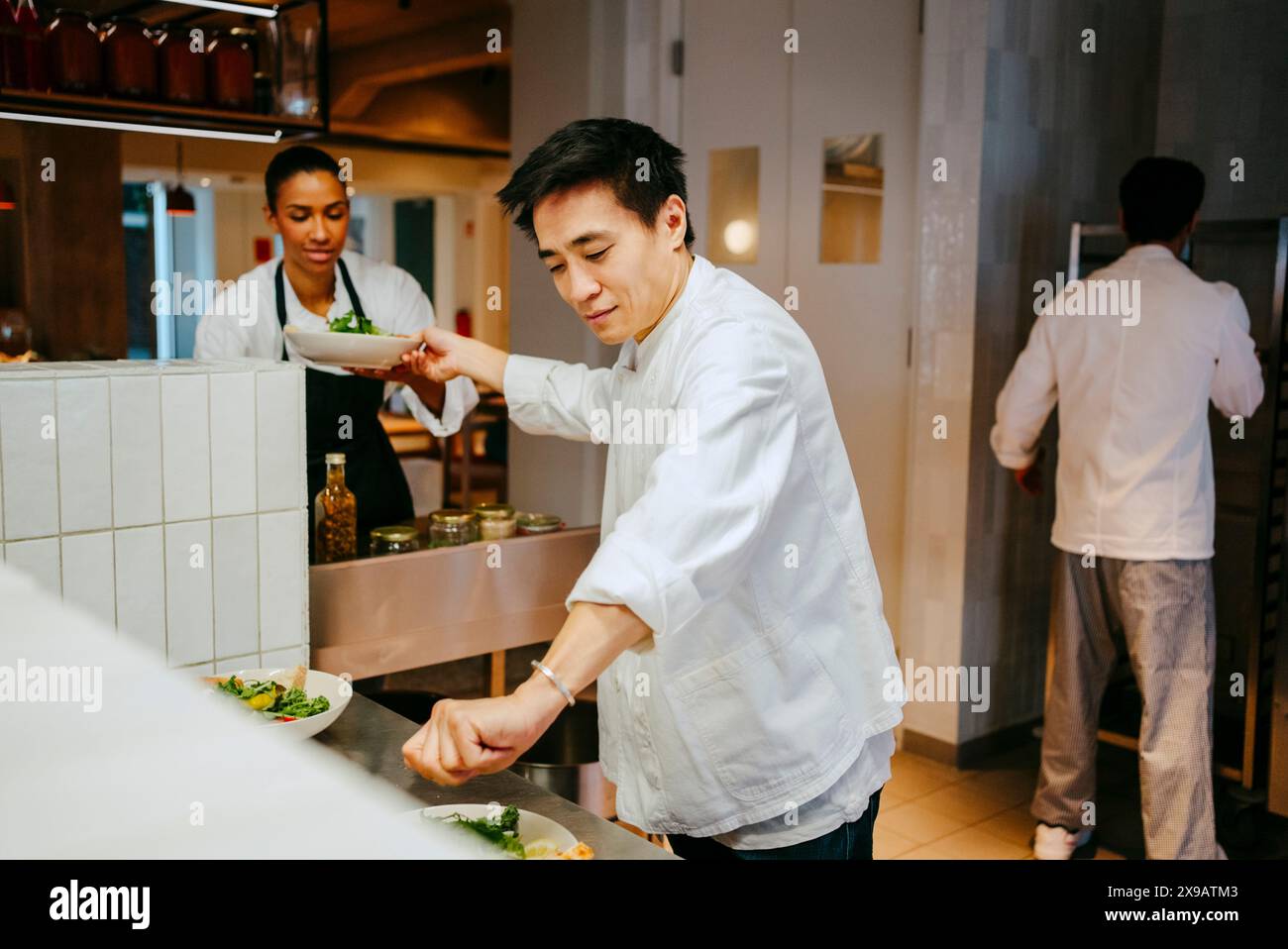 Male chef passing salad bowl to female coworker while finishing salad ...