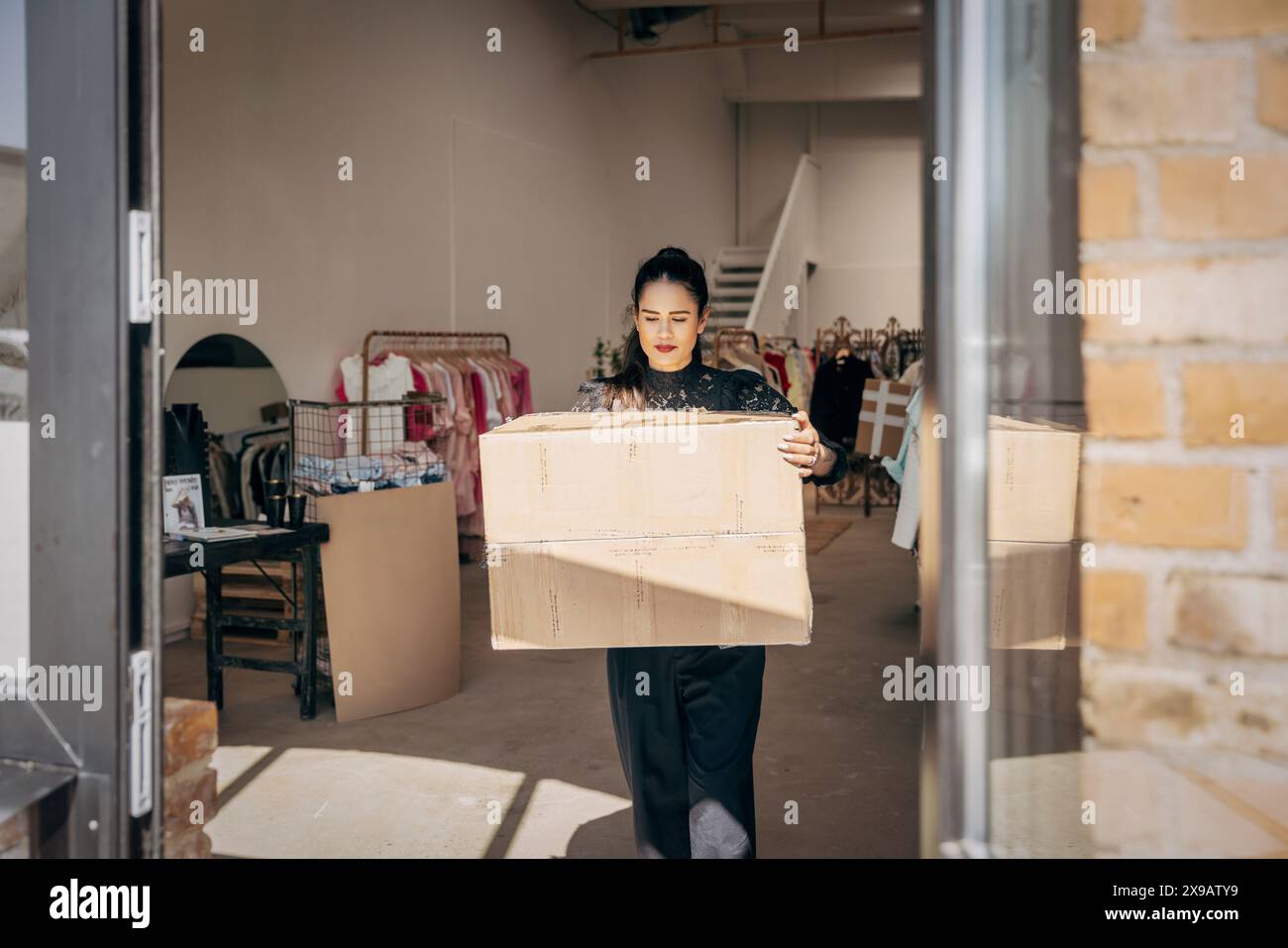 Female owner carrying cardboard box walking towards door in clothing ...