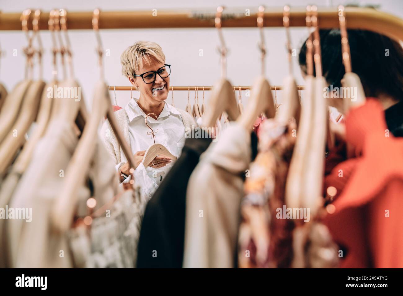 Happy female customer with eyeglasses talking with owner in clothing ...