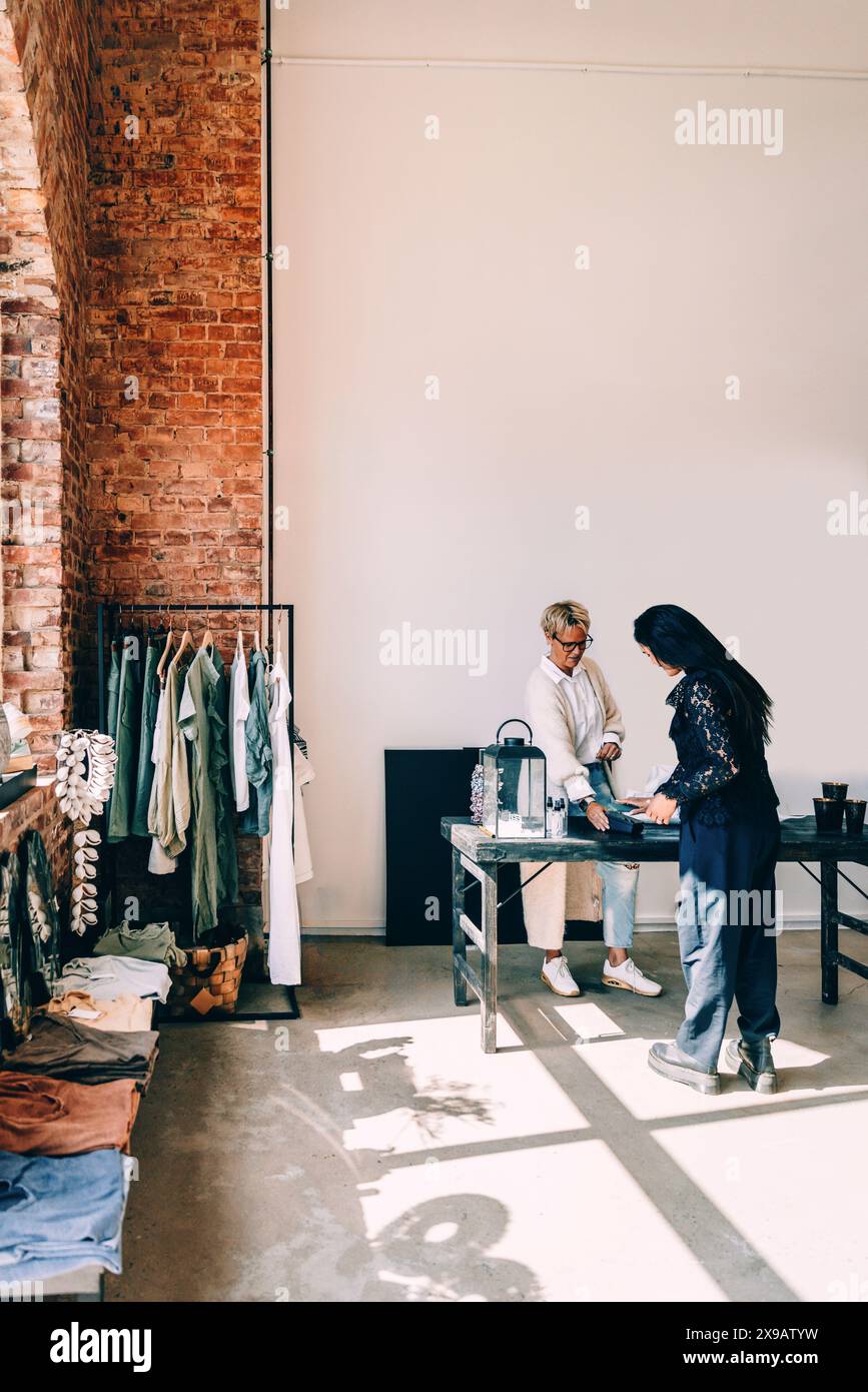Female customer paying via credit card at checkout in clothing store ...