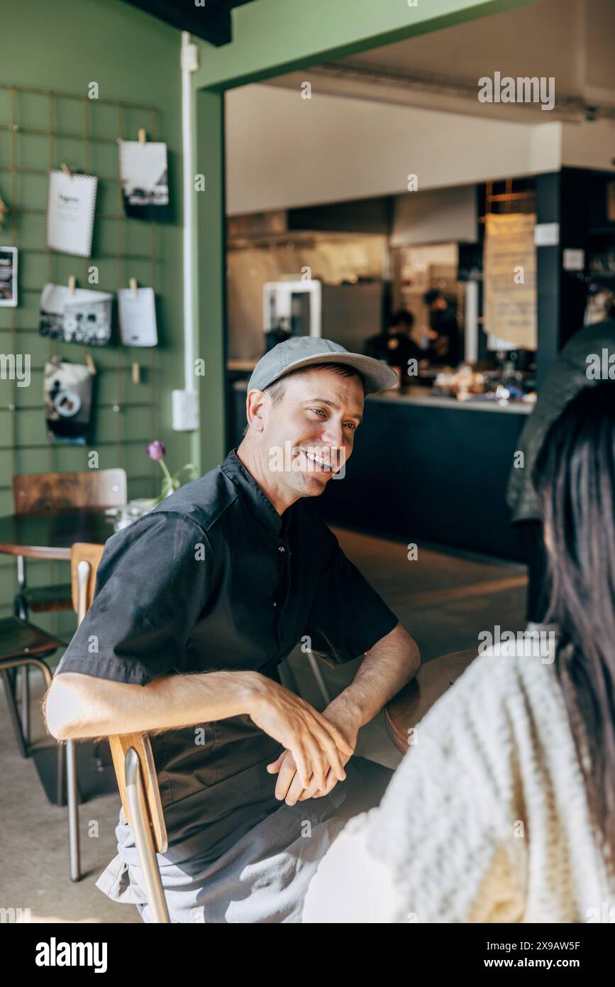 Happy male owner talking with female coworker while sitting at cafe ...
