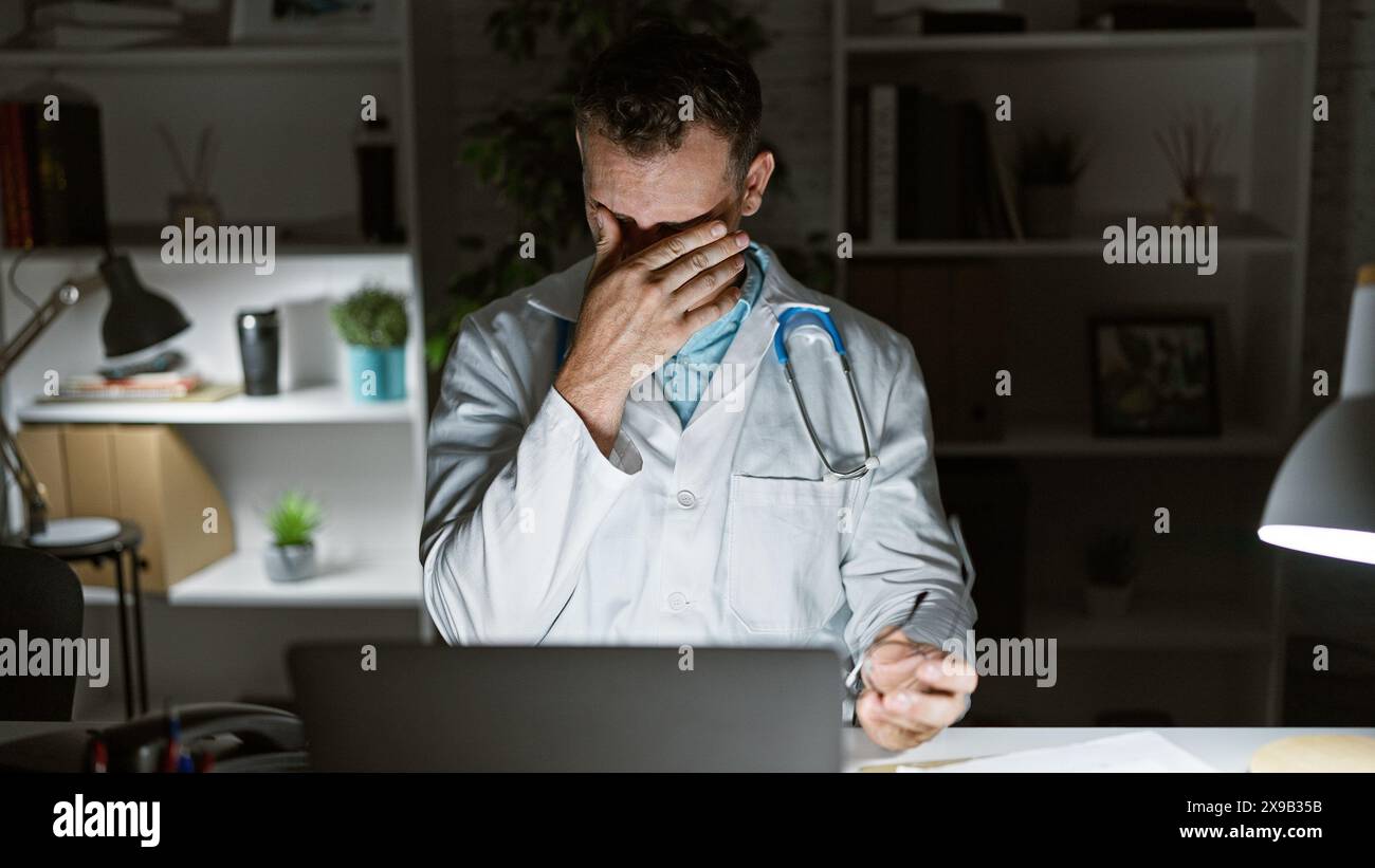 Tired hispanic man in a lab coat with stethoscope in a clinic room ...