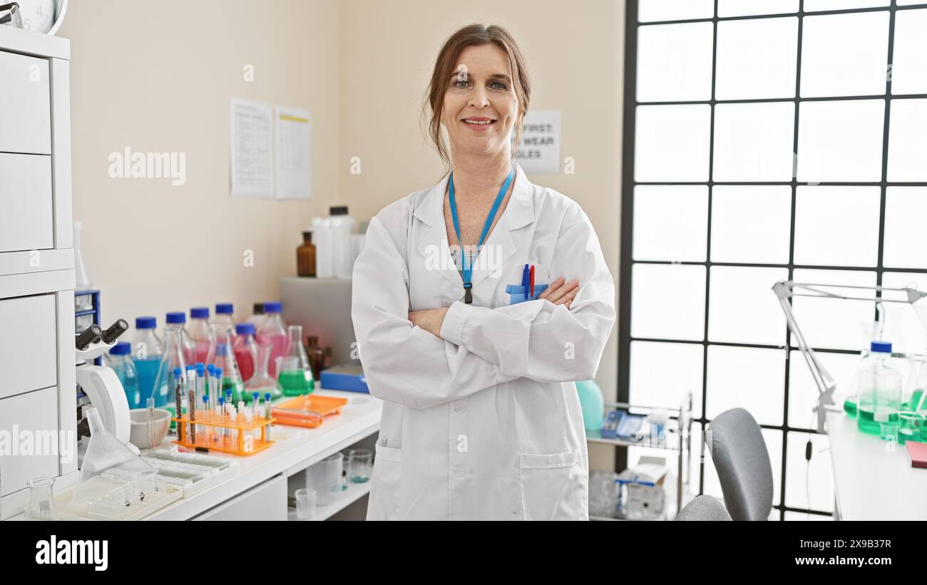 Confident middle-aged woman in lab coat stands with arms crossed in a ...