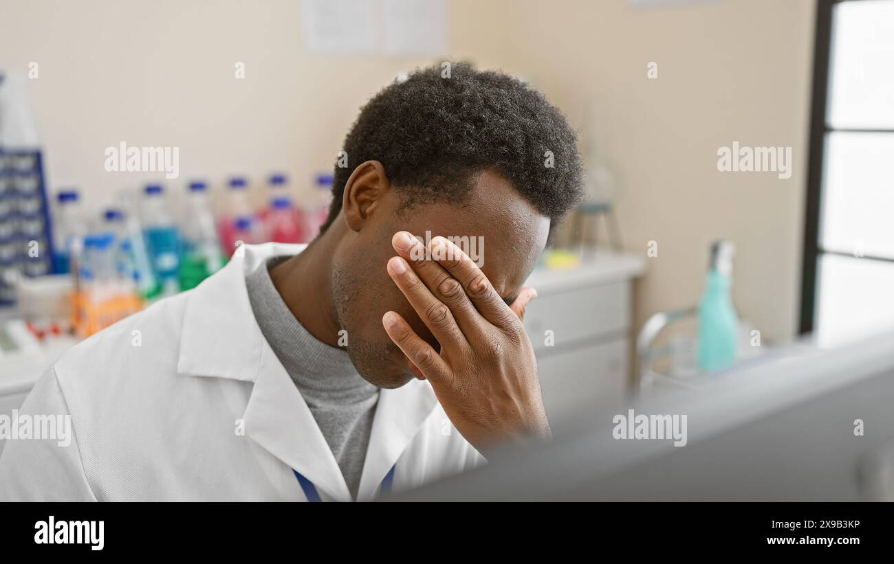 Tired african american man in a white lab coat resting head indoors at ...