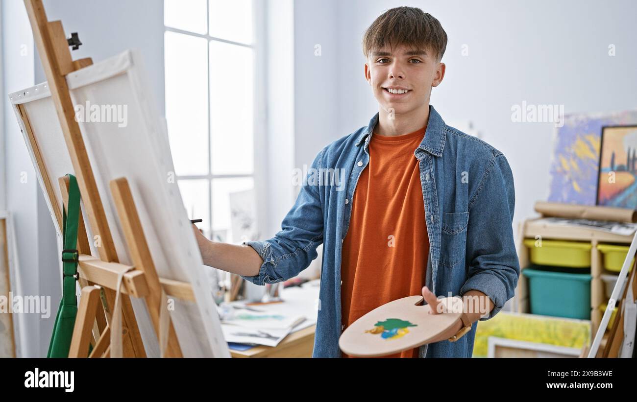 A smiling young caucasian male artist painting on canvas in a bright ...