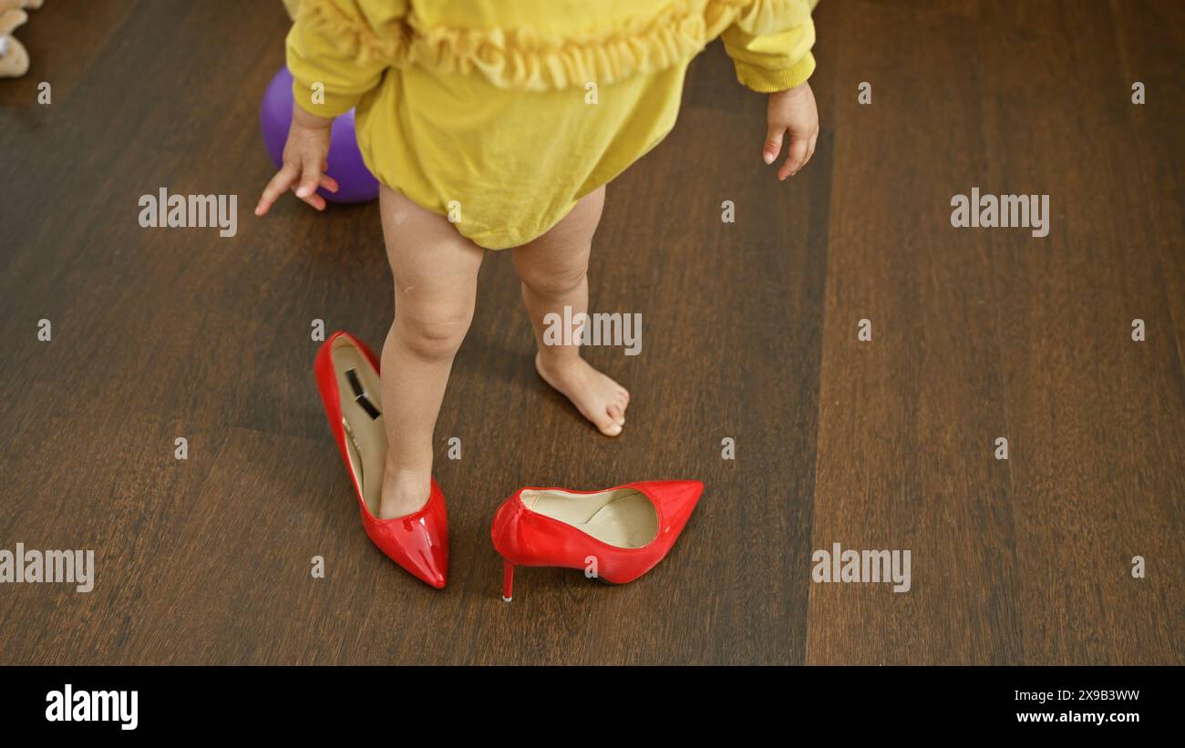 A little girl in a yellow dress plays with oversized red high-heels in ...