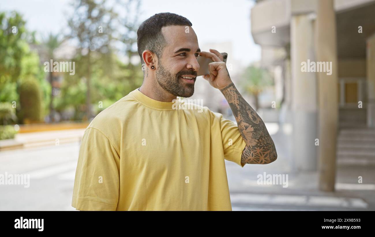 Handsome hispanic man with beard and tattoos smiling outside in an ...