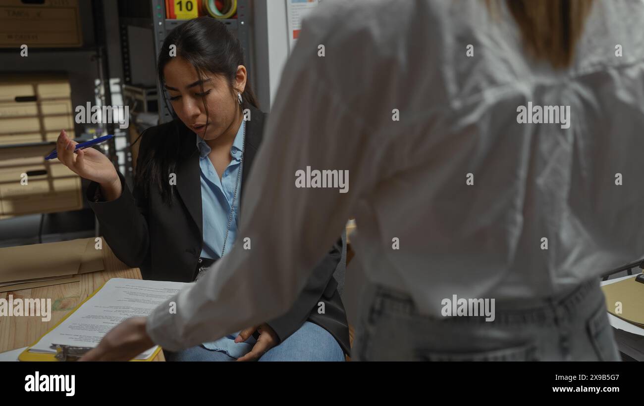 Two women collaborating in a police station office surrounded by files ...