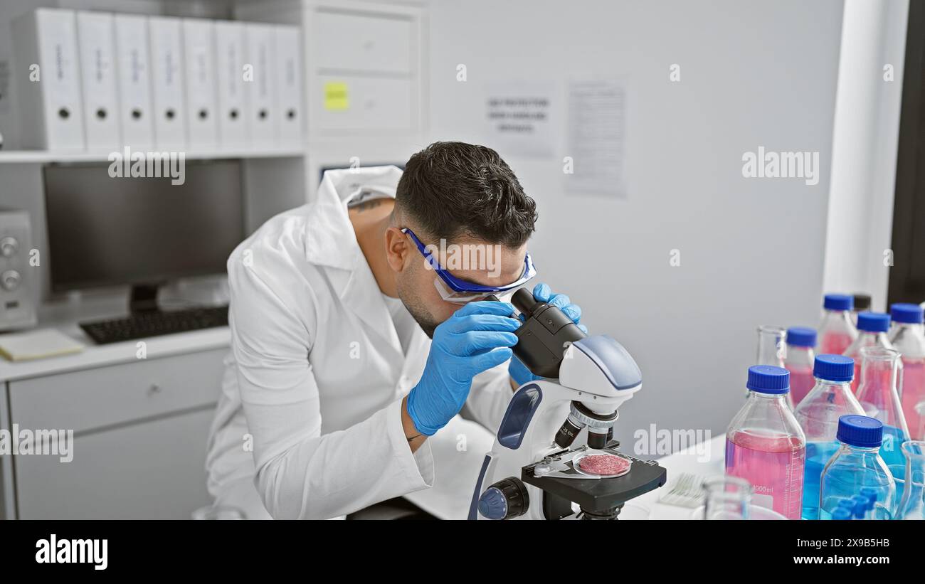A young man examines specimens under a microscope in a laboratory ...