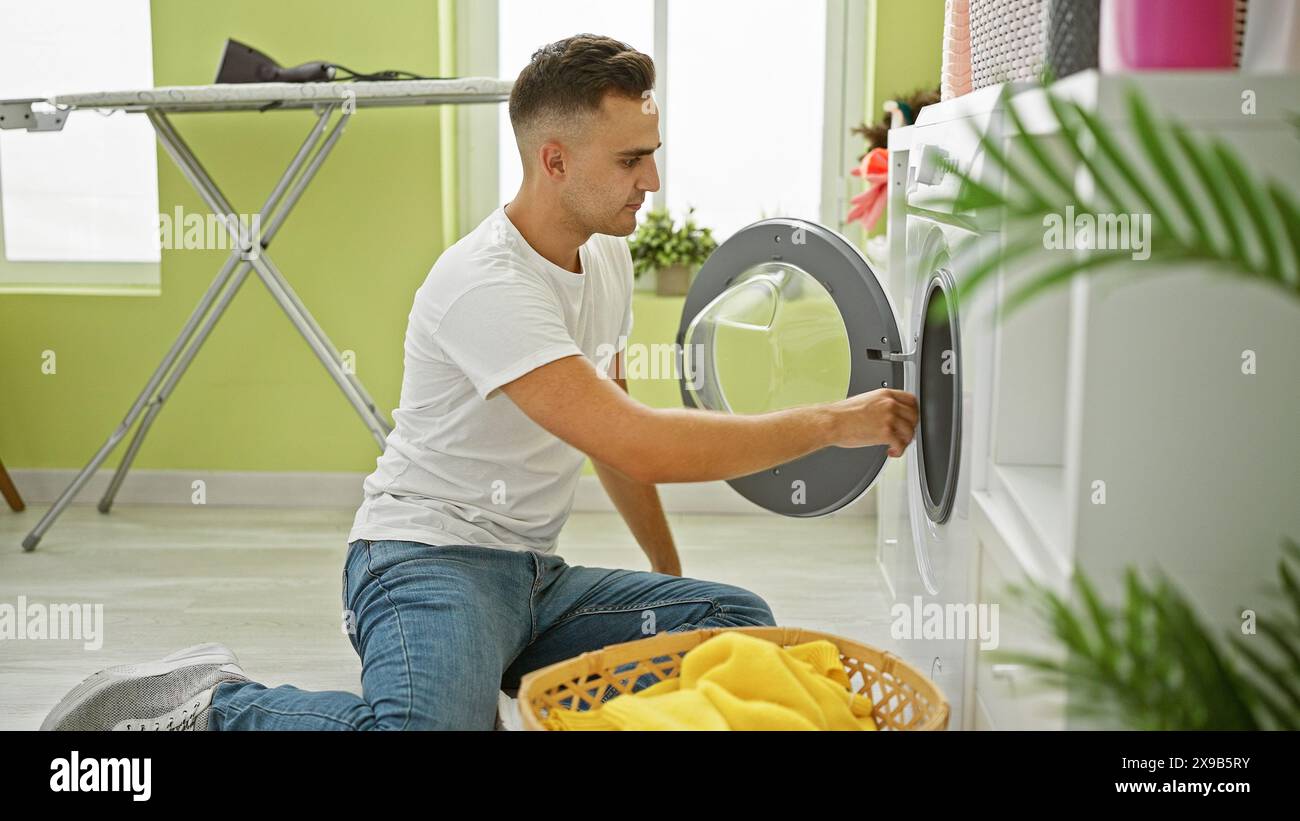 A young man is loading laundry into a washing machine in a bright home ...