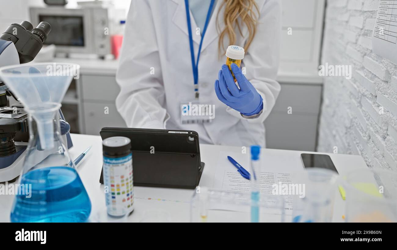 Blonde woman examines specimen in laboratory with microscope, flasks ...