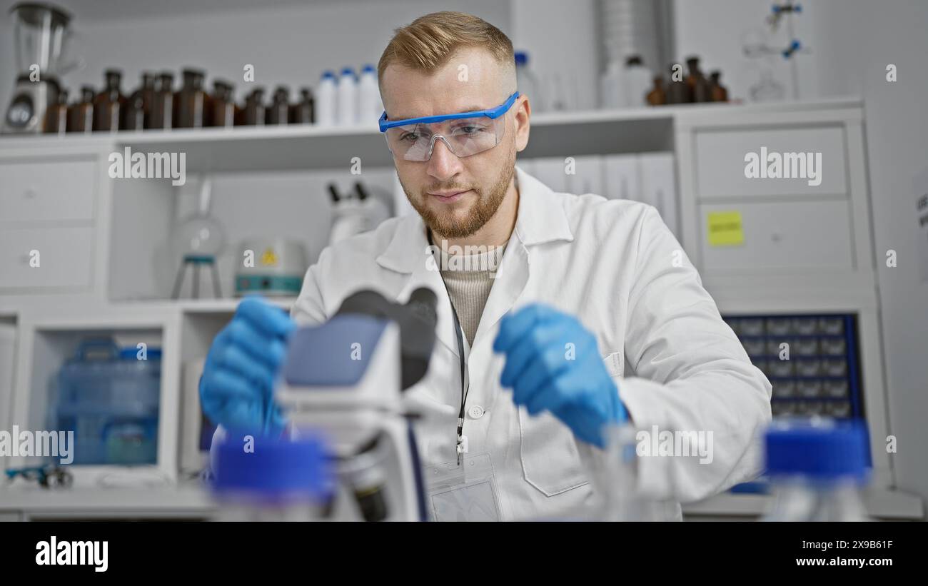 A focused young man in lab coat conducts experiments in a modern ...