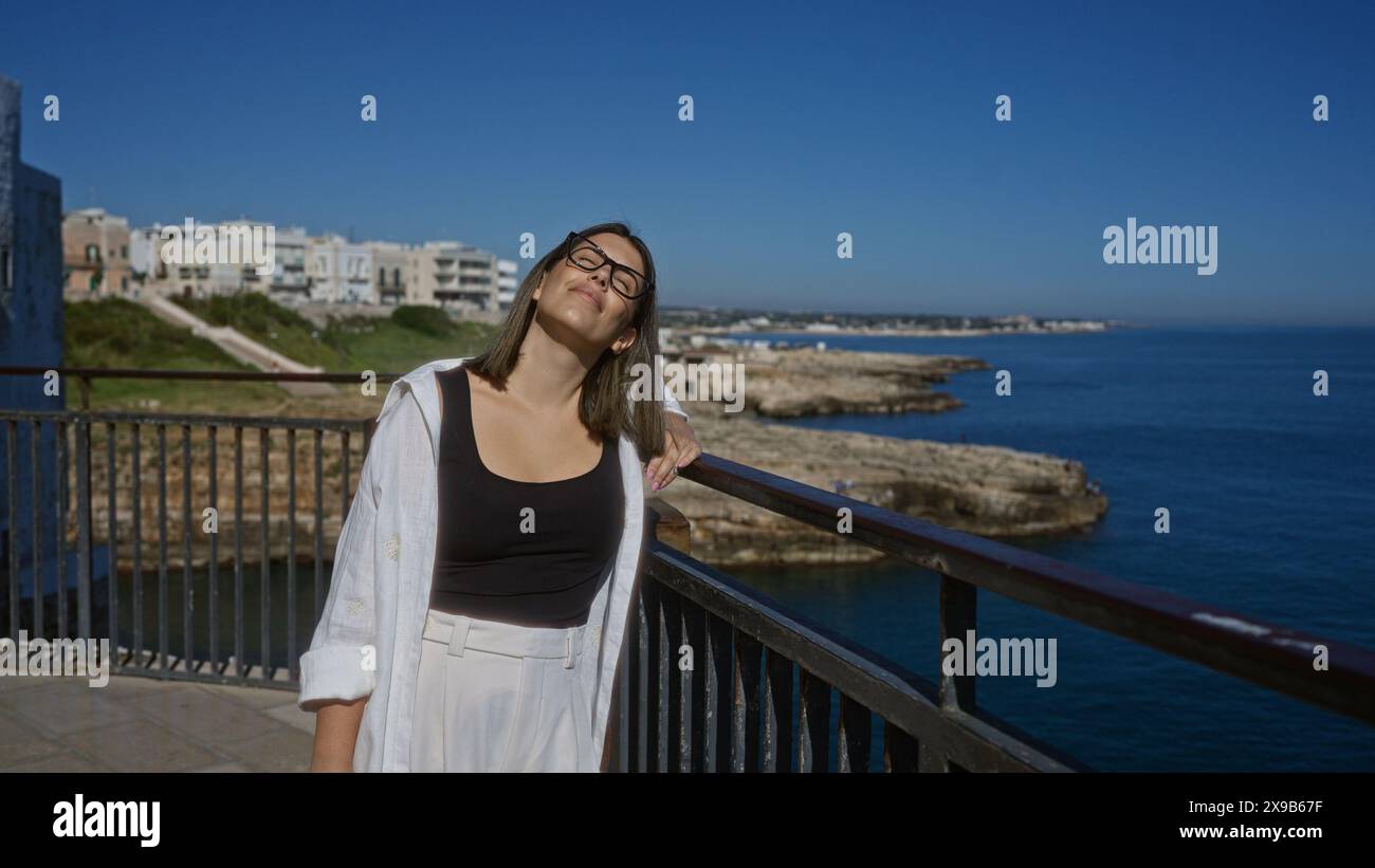 A young hispanic woman enjoys the viewpoint in polignano a mare, puglia ...