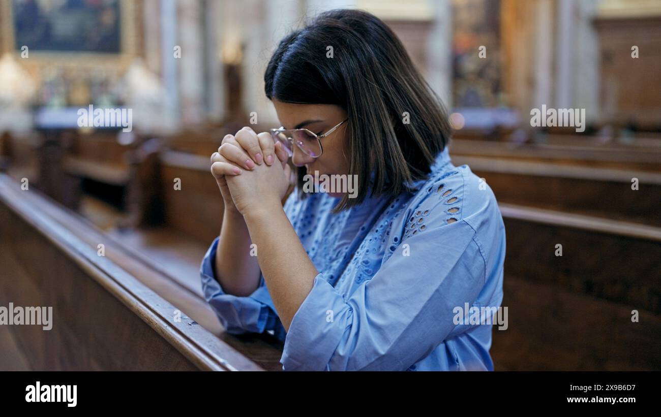 Young beautiful hispanic woman praying on a church bench at St. Karl ...