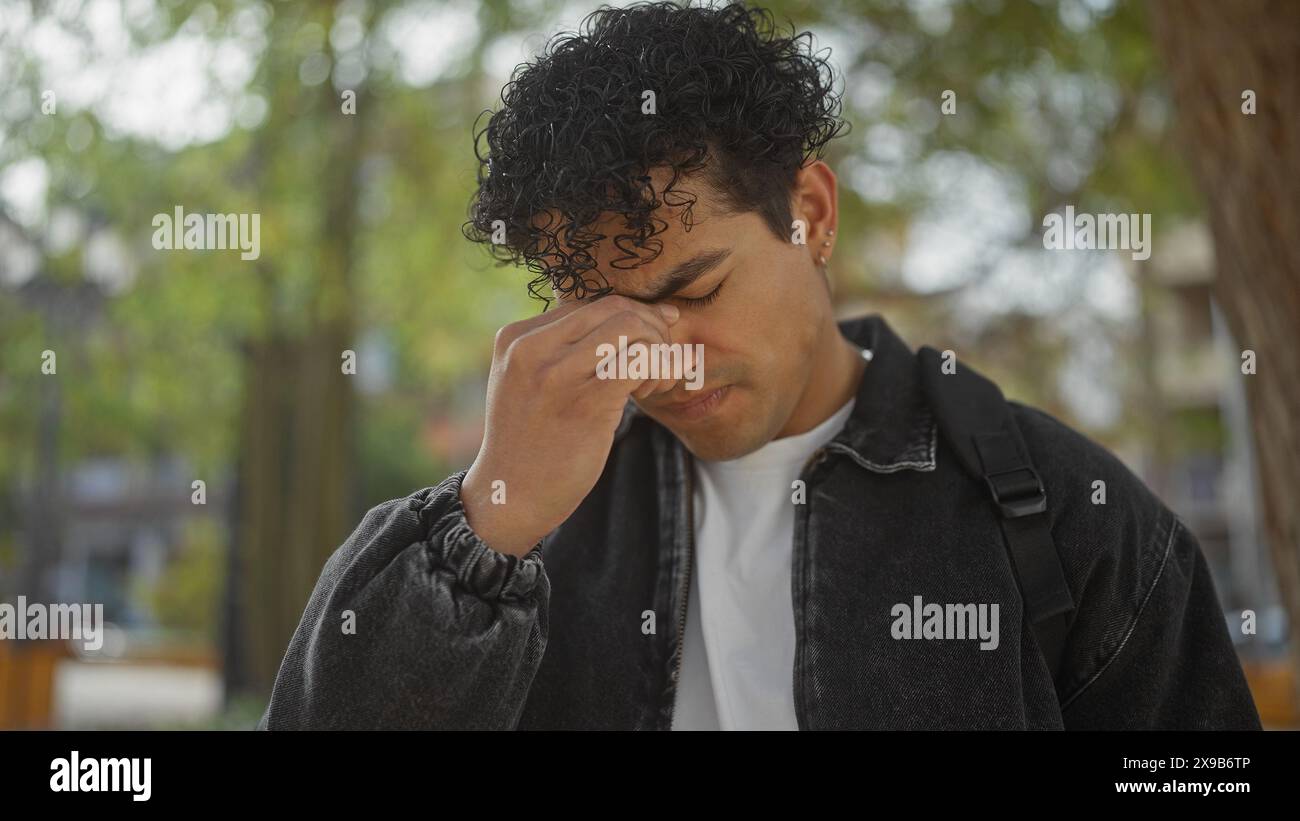 A stressed young hispanic man in casual attire rubbing his eyes in a ...