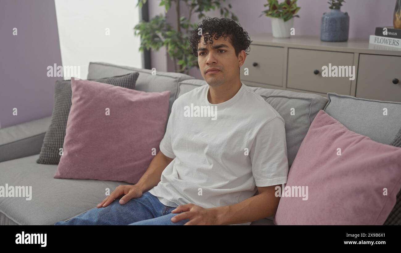 A thoughtful hispanic man sits relaxed in a modern living room with ...