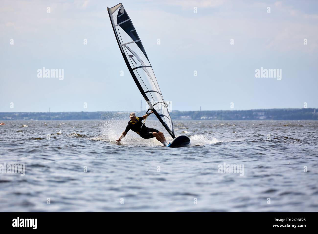 Young man surfing the wind and touching water surface with splashes ...