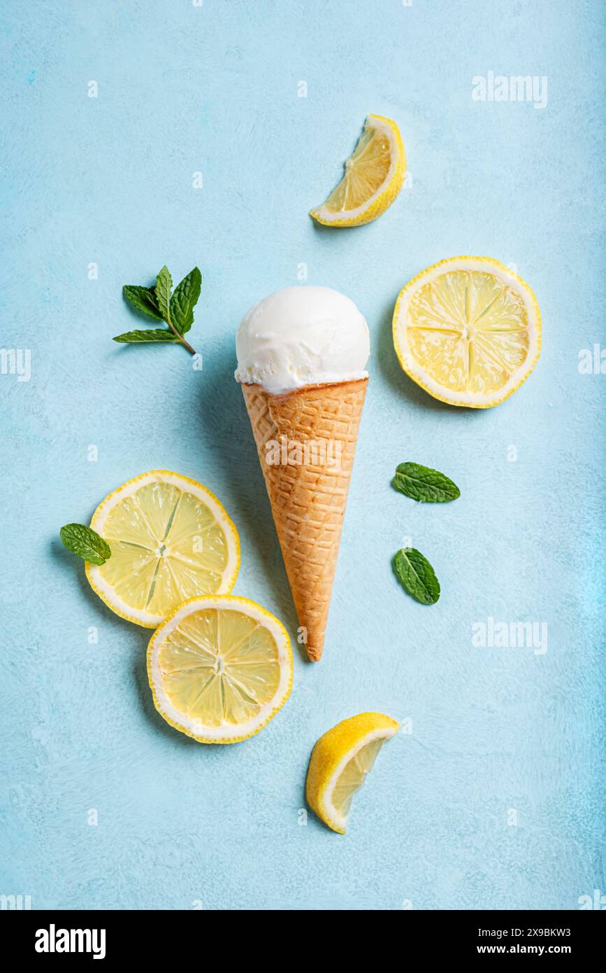 Scoop of lemon ice cream in wafer cone and lemon slices on light blue ...