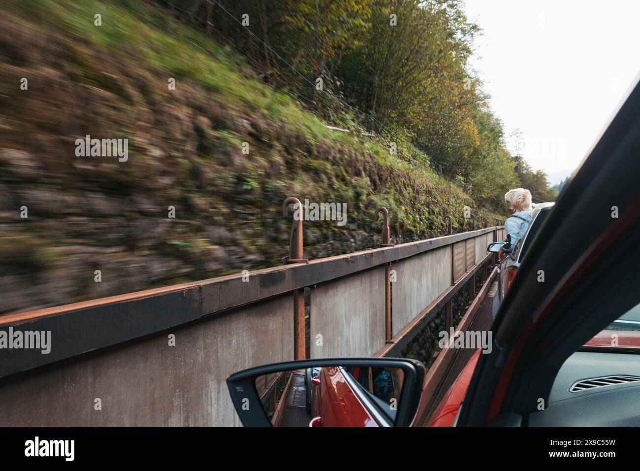 A boy leans out a car window as it travels on the back of a motorail ...