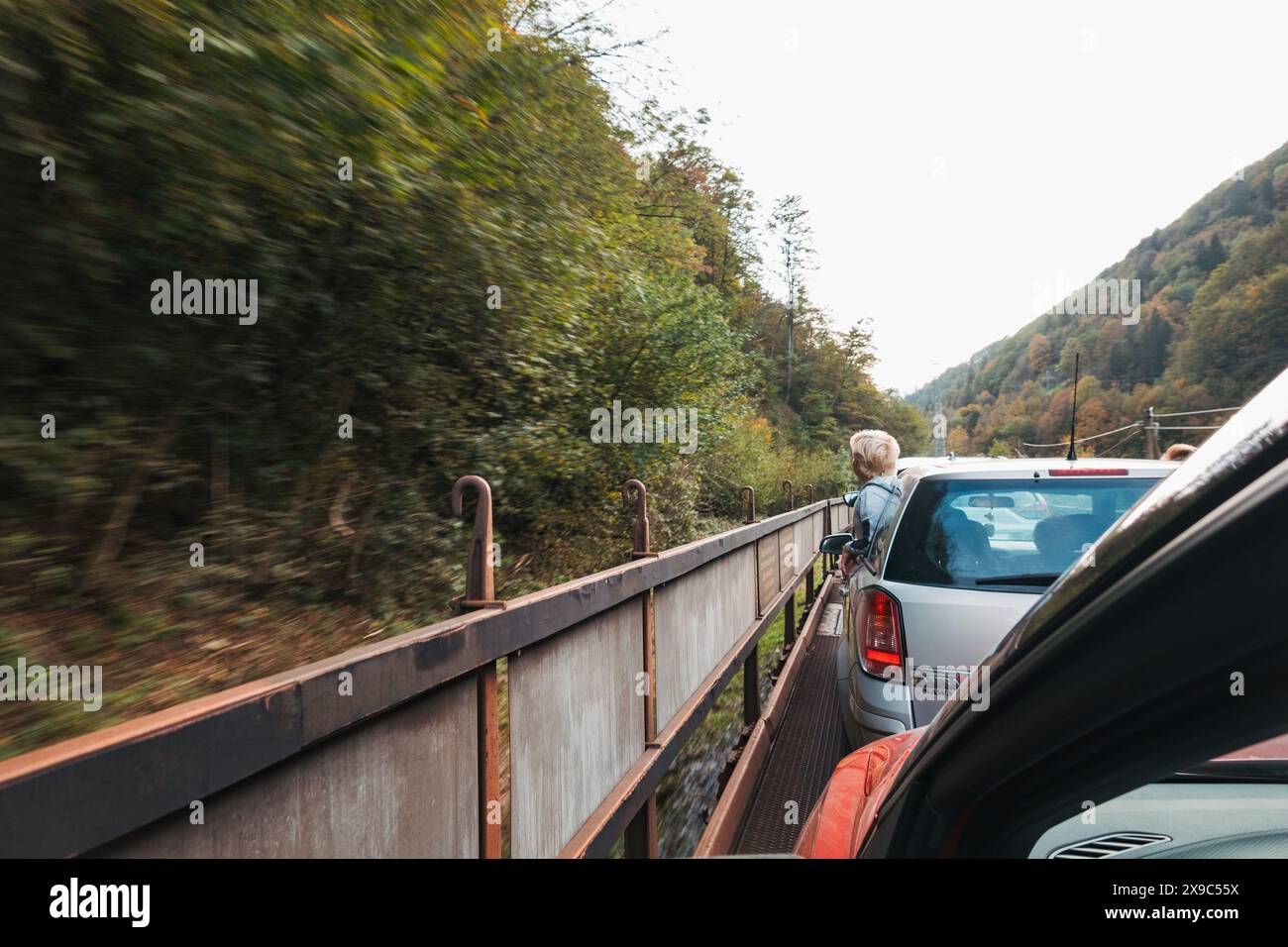 A boy leans out a car window as it travels on the back of a motorail ...