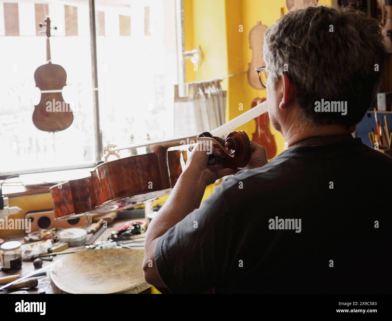 From behind, a luthier works intently on a cello in a well-organized ...