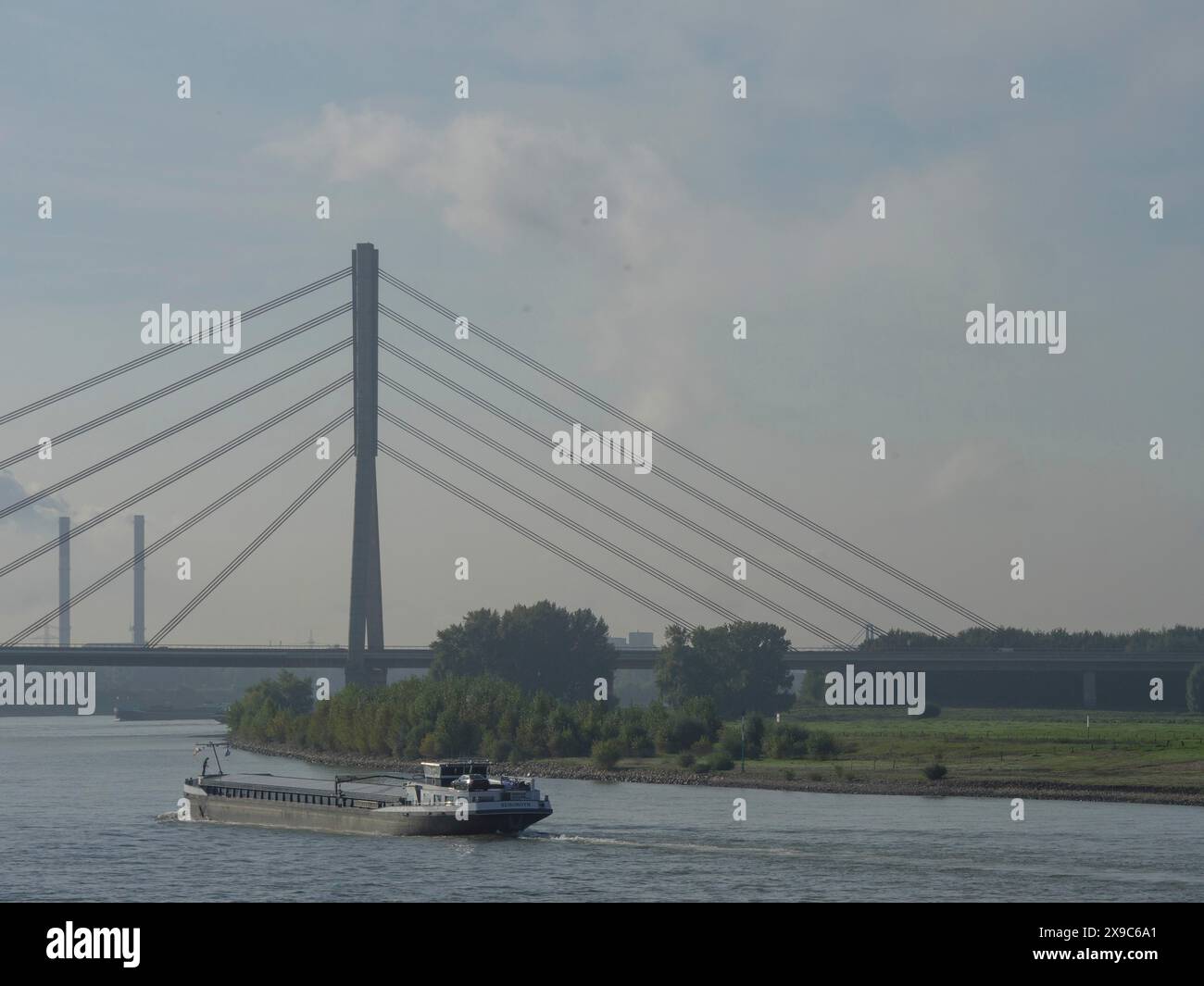Ship sailing under a bridge in calm weather with clouds and trees along ...