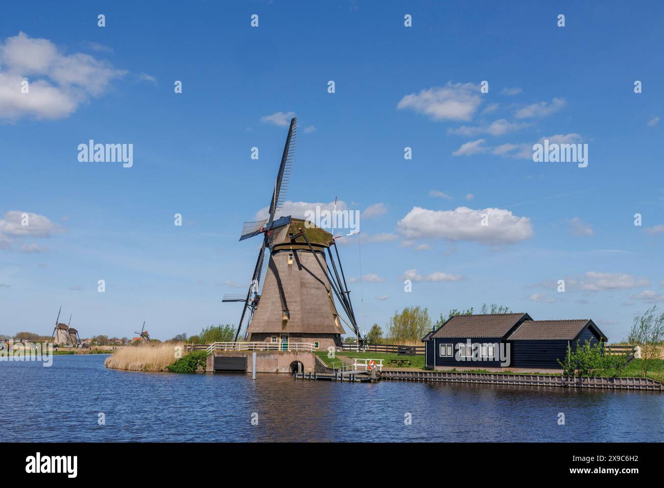 Rural scene with an old windmill on a lake and a small blue house under ...