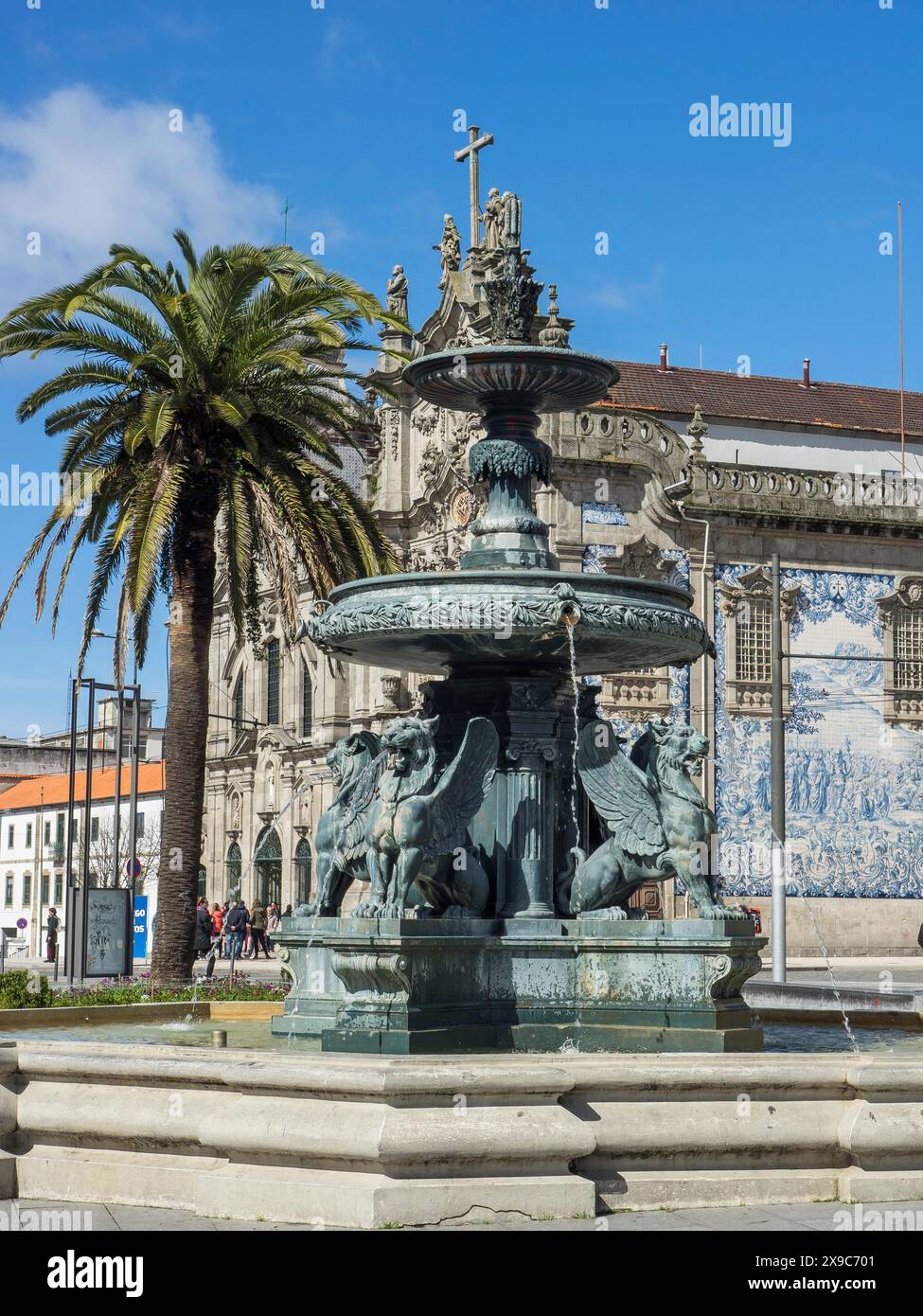 Ornamental fountain with mythological figures, large palm tree and baroque church in the ...