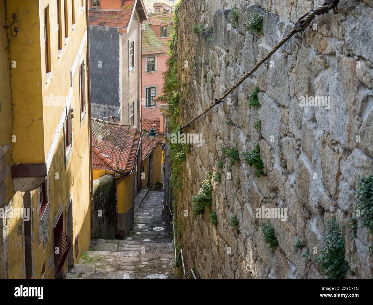 Narrow cobbled alley between yellow houses and a stone wall with ...