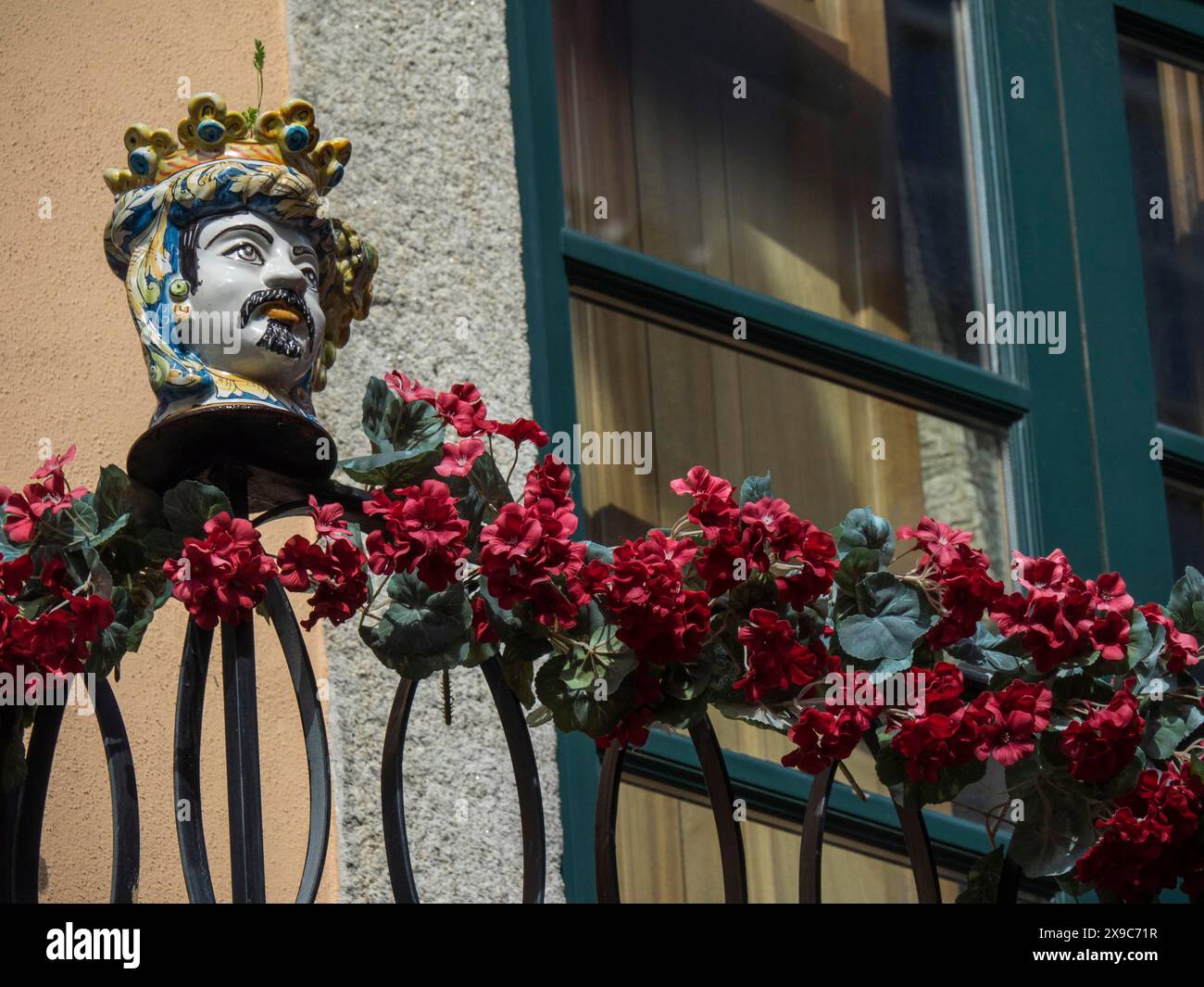 Ceramic bust on a balcony with red flowers in front of a window on a ...