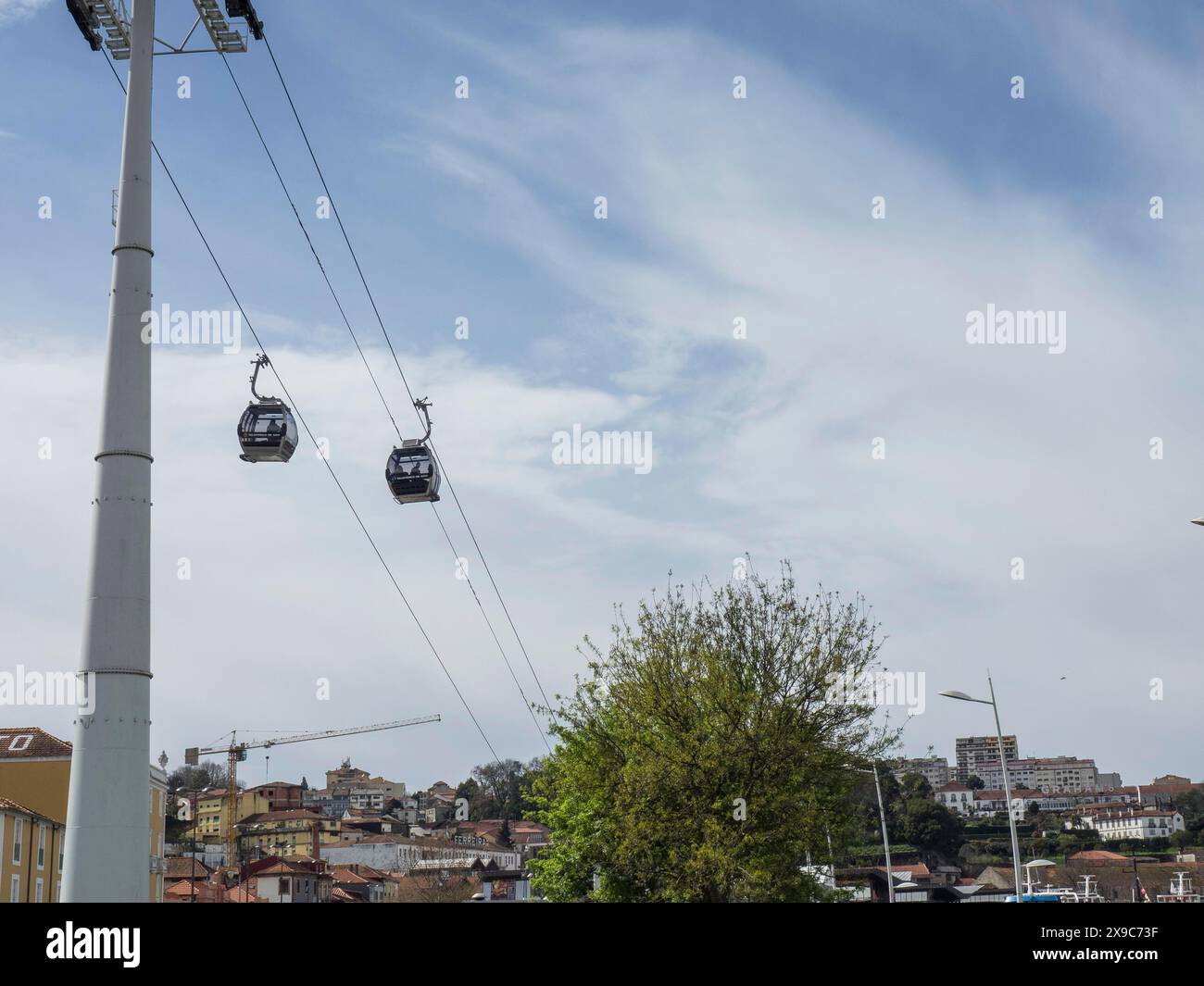 Cable car gondolas crossing a tree, houses and cable car support in the background, cloudy sky ...