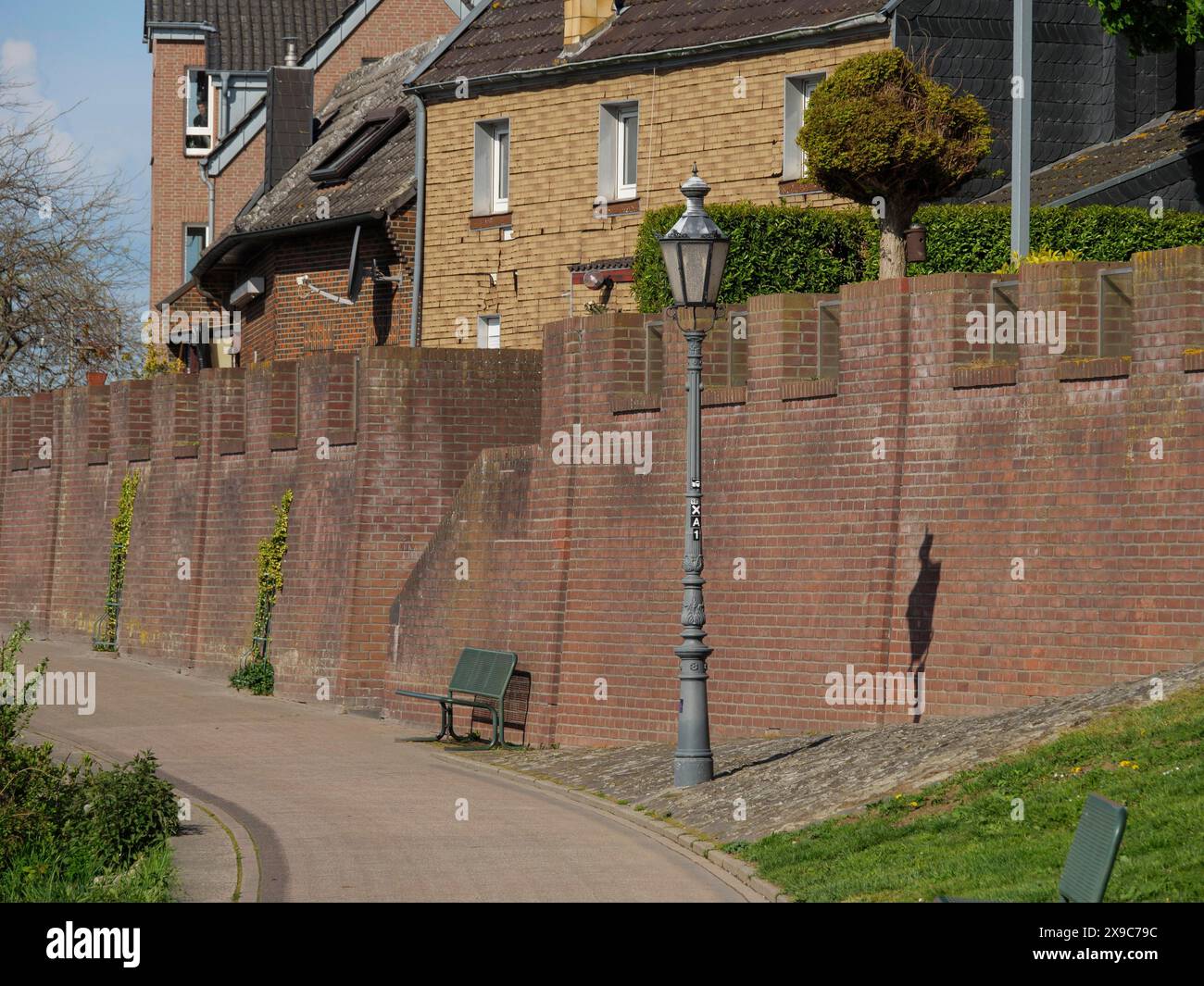Pavement along a brick wall with houses behind and a street lamp in the ...